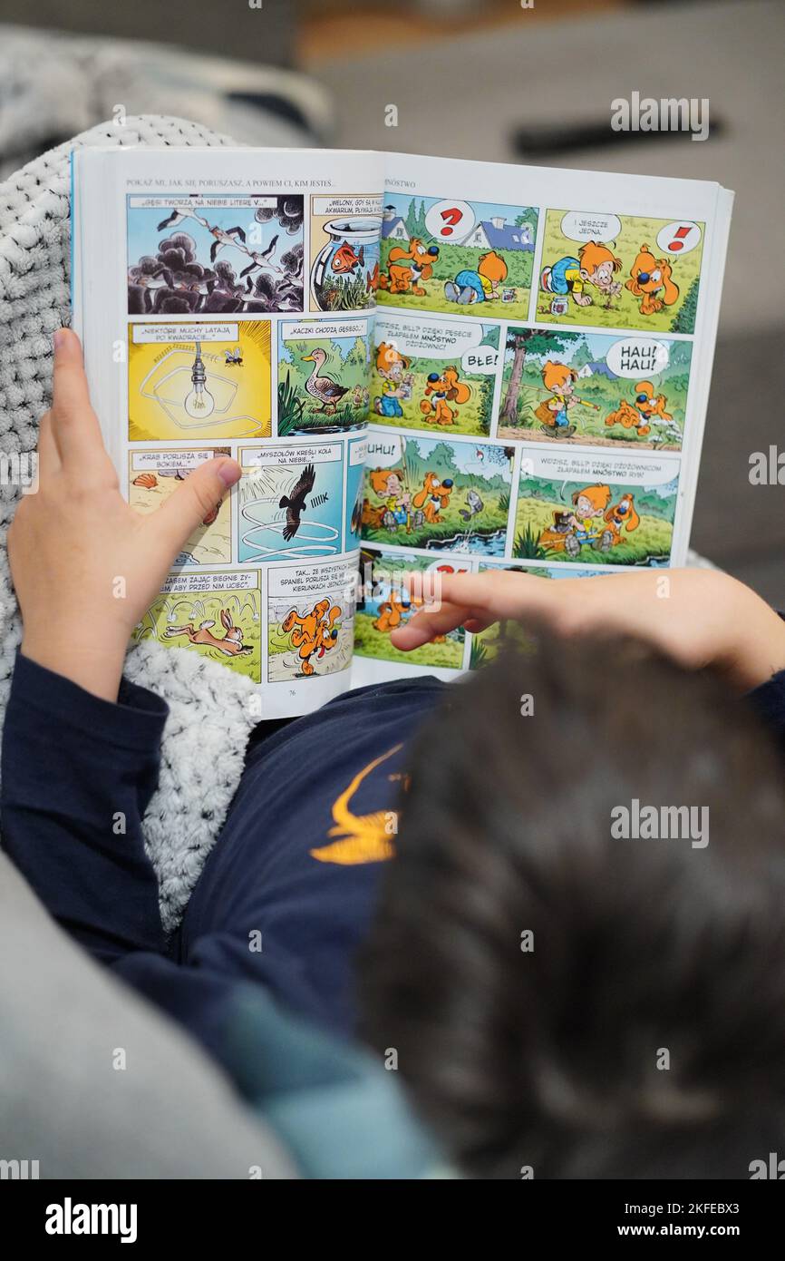 A child reading a Polish Ptys I Bill comic book on a sofa in a living ...