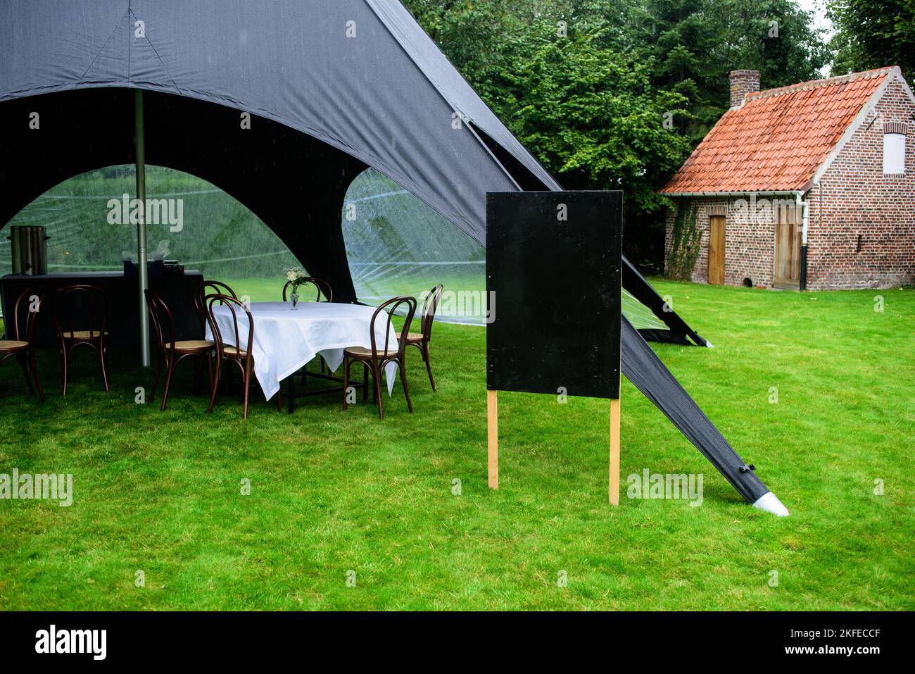 black tent in a garden with dressed tables waiting for people and a ...