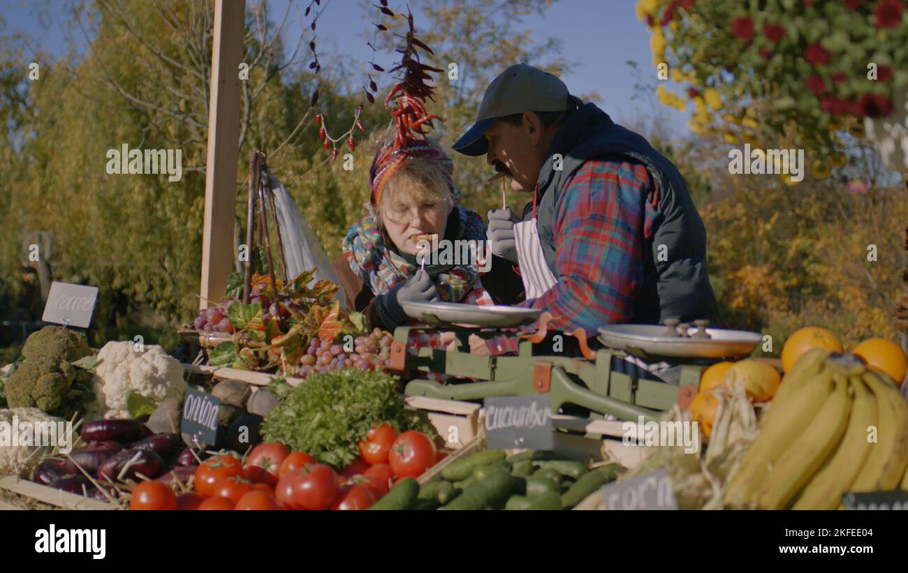 Couple of elderly farmers making lunch break, tasting meat cooked by ...