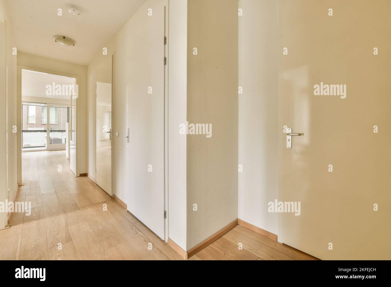Narrow corridor with white walls and doors leading to spacious room ...