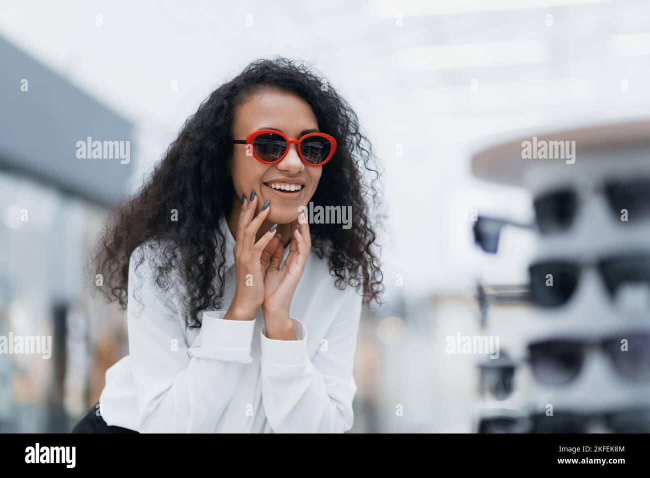 young woman is looking thoughtfully at a display case with sunglasses ...