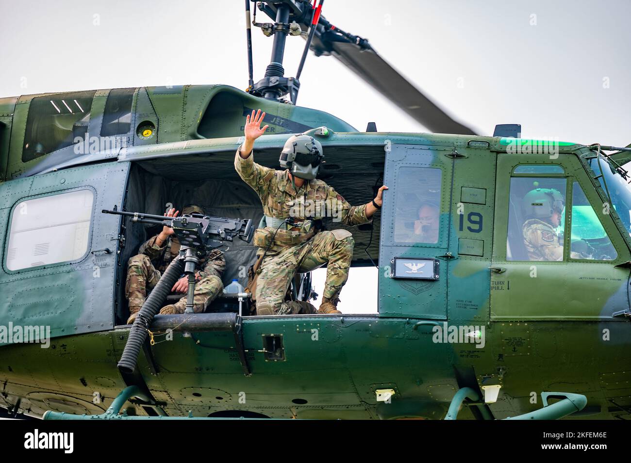 A member of a flight crew waves as a UH-N1 Huey takes off during the ...