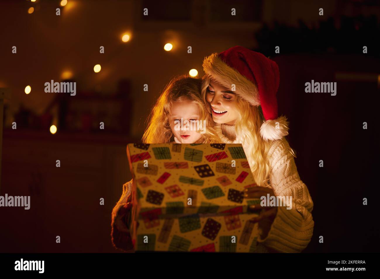 Front view of blonde mother wearing christmas hat opening present, gift ...