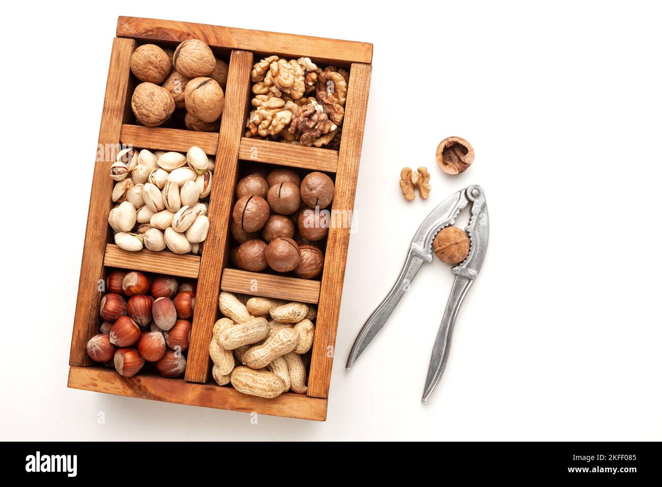 Different nuts in a wooden box and a nut cracker on a white background ...