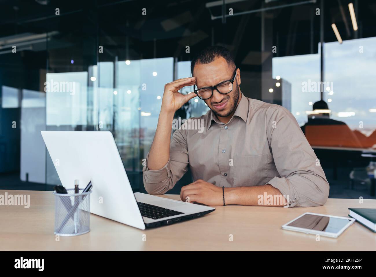 Sick man at work working using laptop, african american man having ...