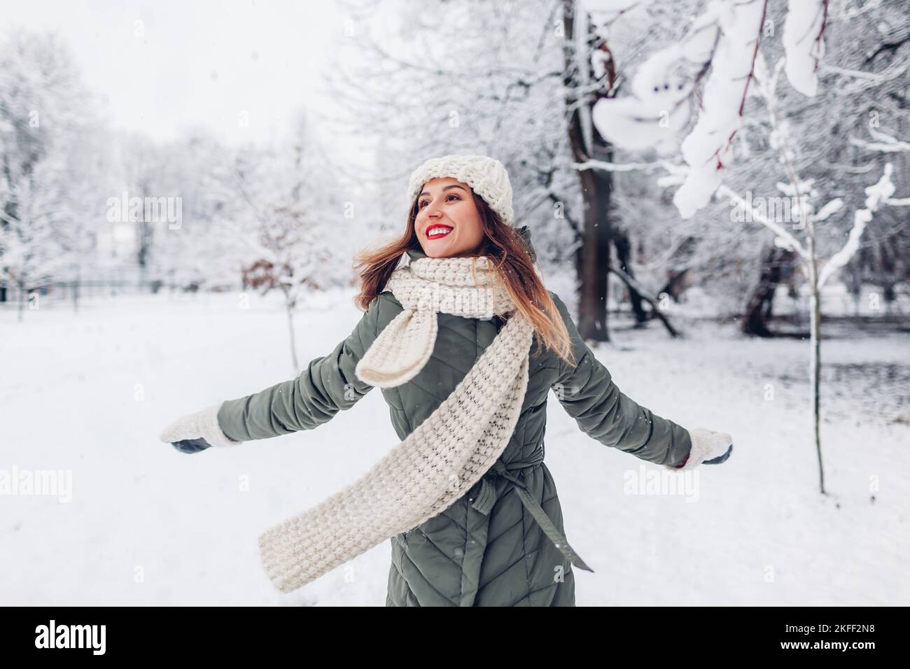 Happy young woman spinning in snowy winter park wearing warm knitted ...