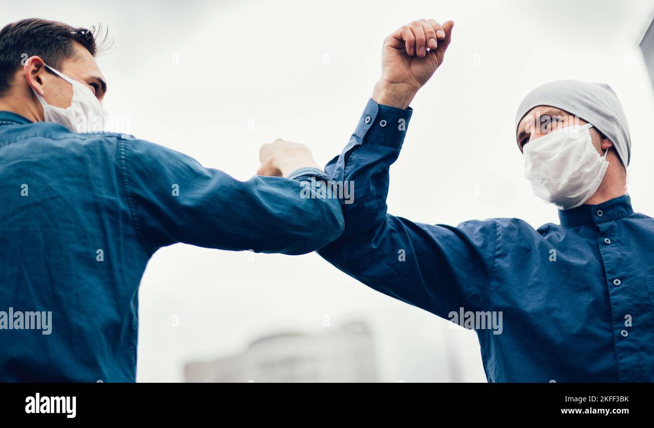 two friends greeting each other with their elbows on a city street ...
