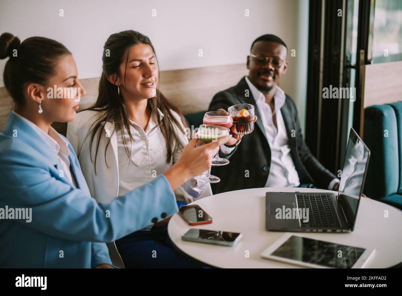Three business colleagues making cheers with their drinks while sitting ...