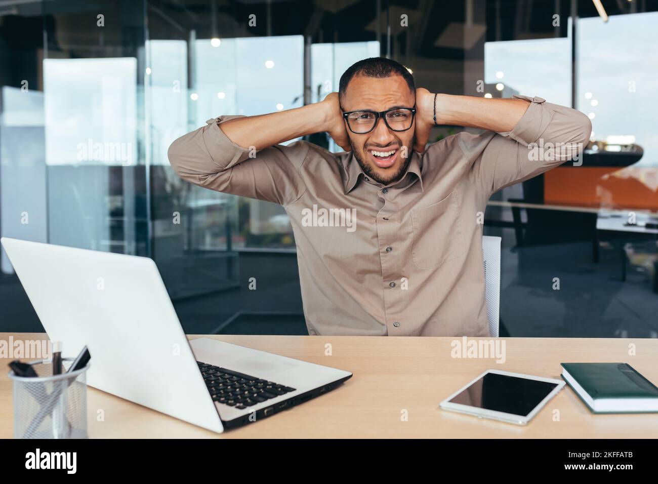 worried office worker looks at the camera and covers his ears with his ...