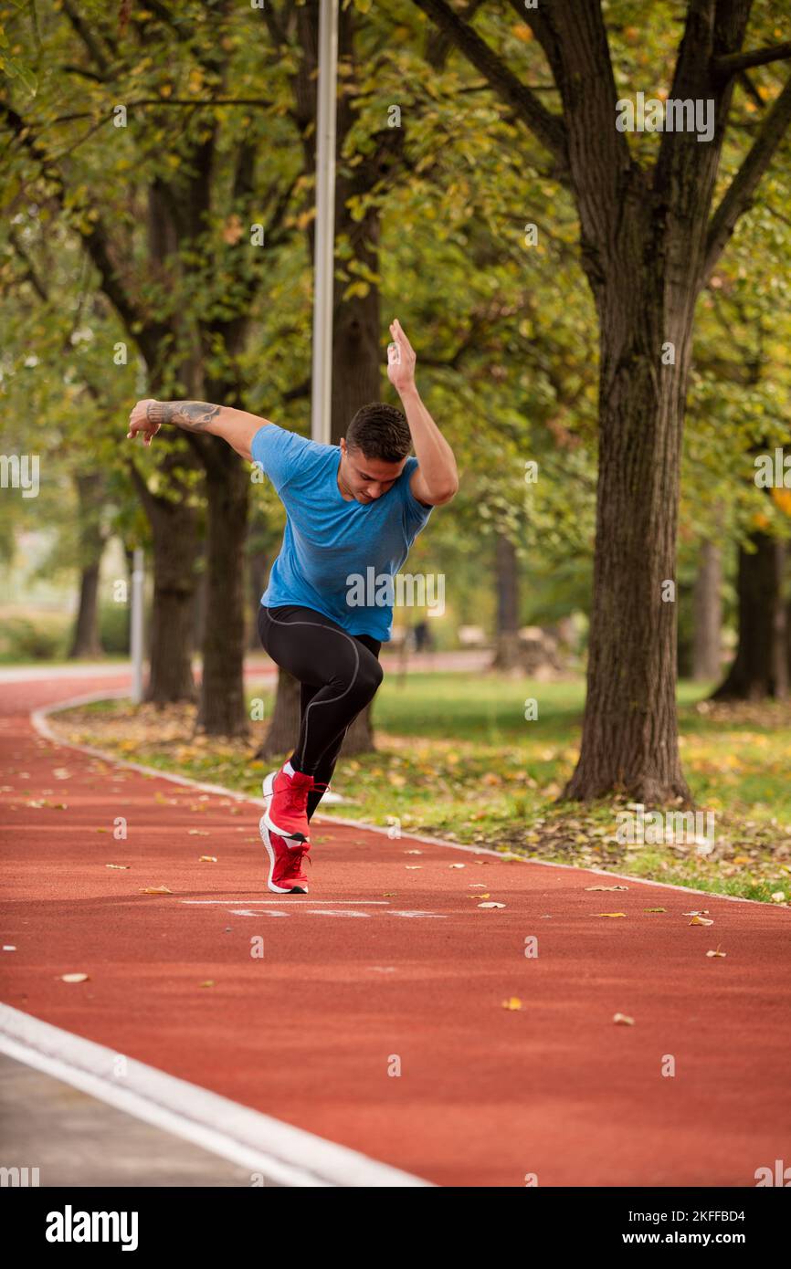 Attractive and handsome guy is doing a sprint start on the red track ...