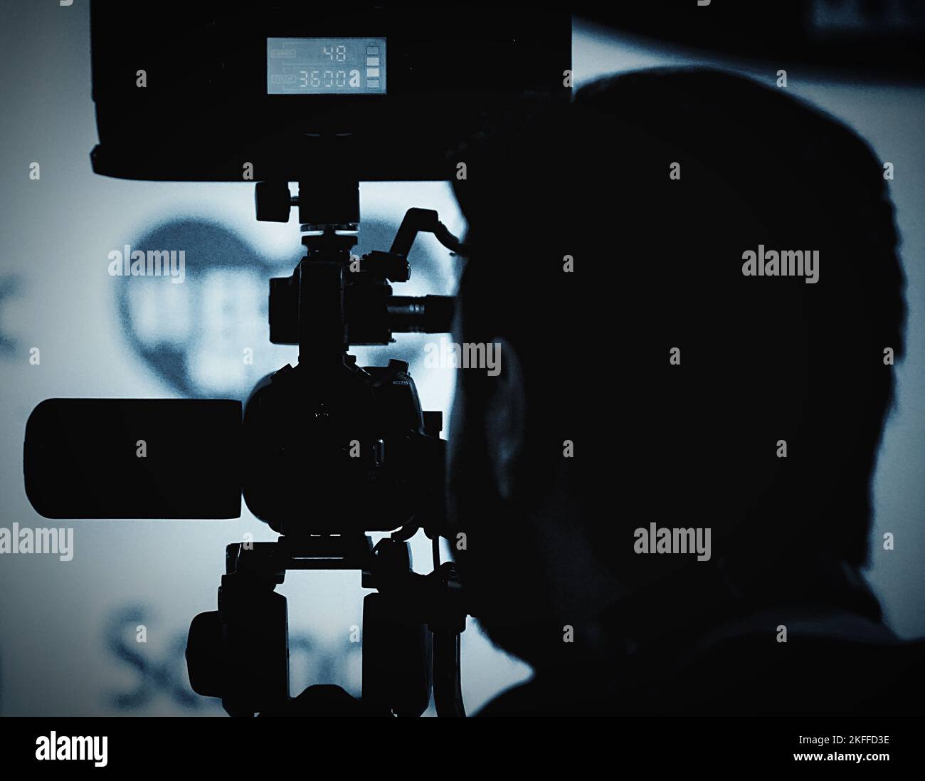 A silhouette of a man using a professional digital camera with a microphone to record a video ...