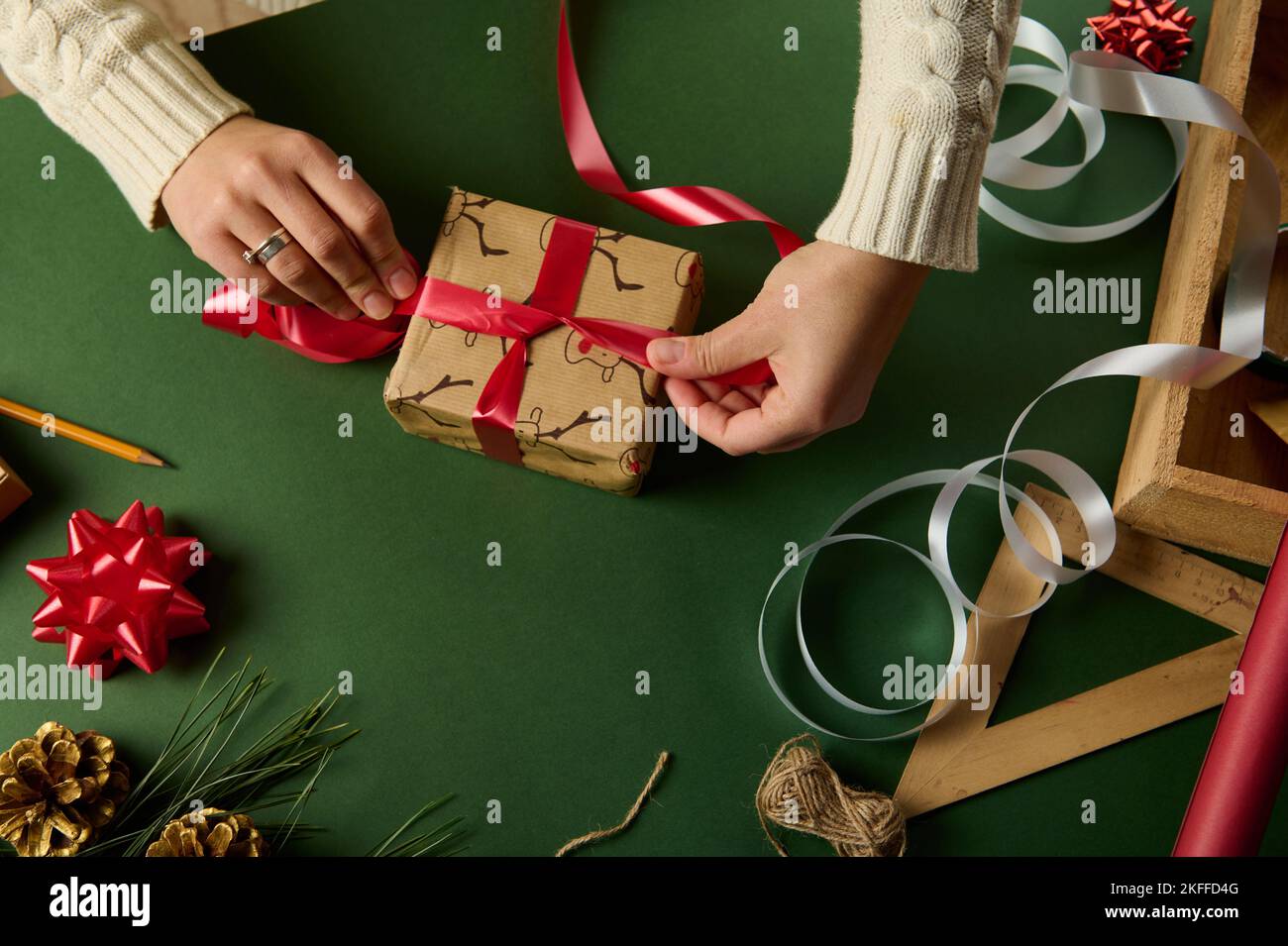 Top view woman ties up a Christmas gift wrapped in wrapping paper with ...