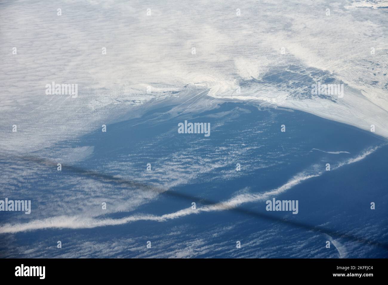 Aerial view from airplane window over clouds to snow covered frozen sea ...