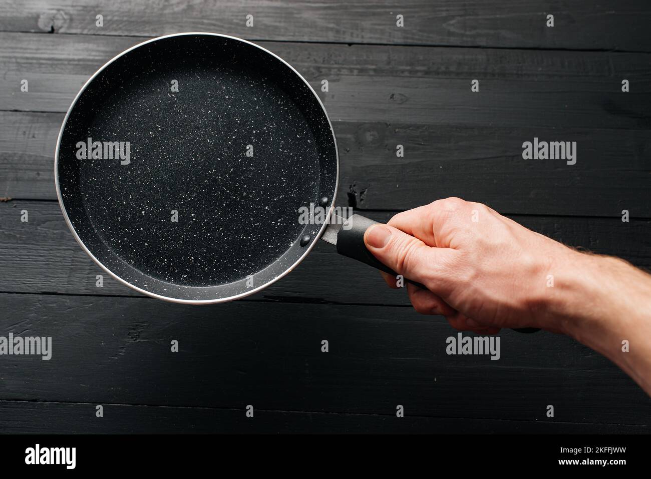Empty pan in hand on black wood background Stock Photo - Alamy