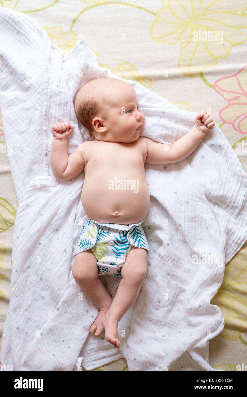 Happy baby girl lying on her back on a bed. She is wearing a modern ...