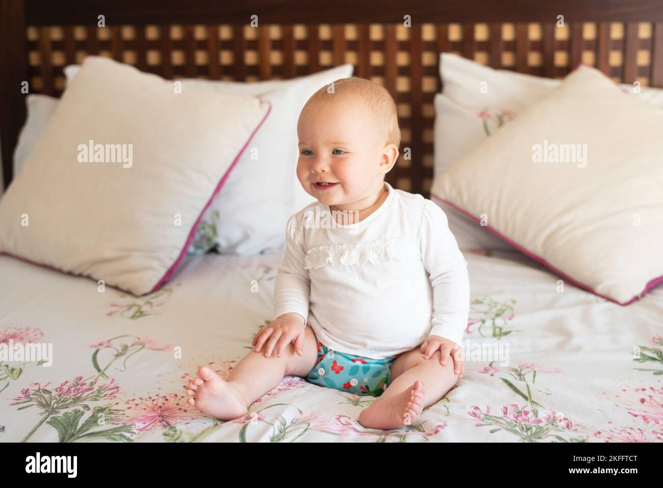 A happy baby girl learning how to sit. She is wearing a modern ...