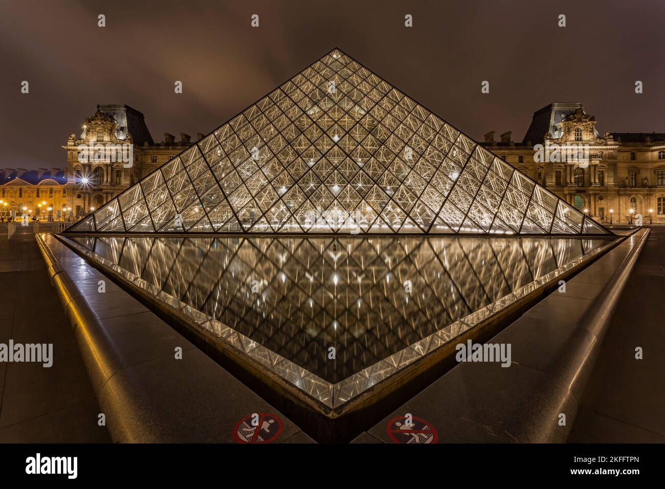 The Louvre Museum Pyramid illuminated at night reflecting symmetrically ...