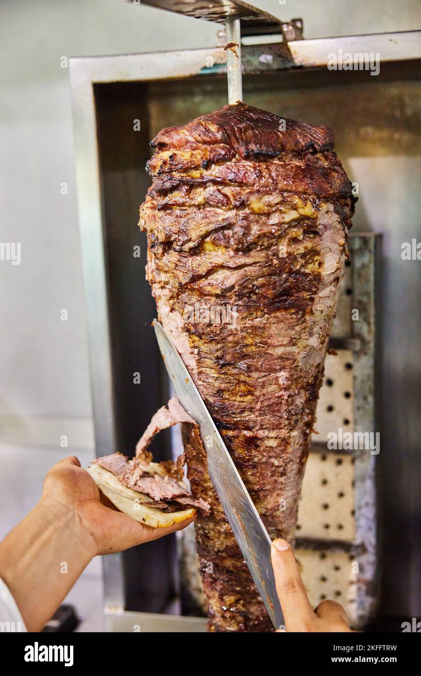 A vertical shot of a cook cutting meat off a spinning doner grill onto ... A vertical shot of a cook cutting meat off a spinning doner grill onto ...
