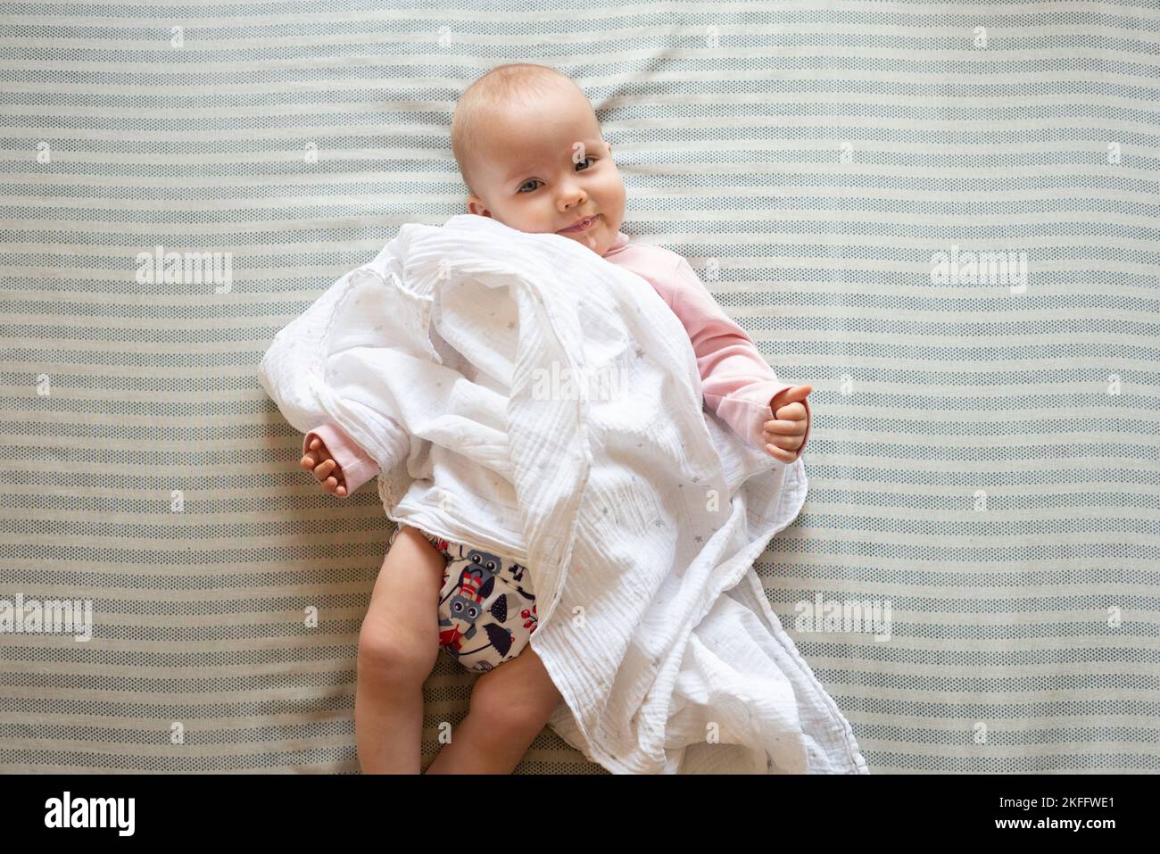 Happy baby girl lying on her back on a bed. She is wearing a modern ...