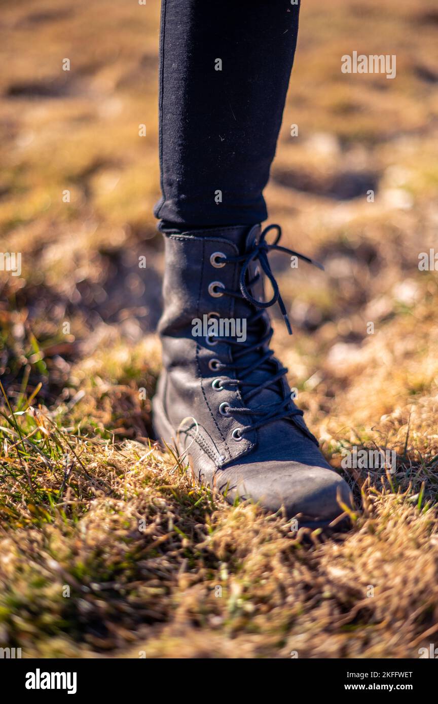 A vertical closeup of a foot with boots standing on a yellowing grass ...
