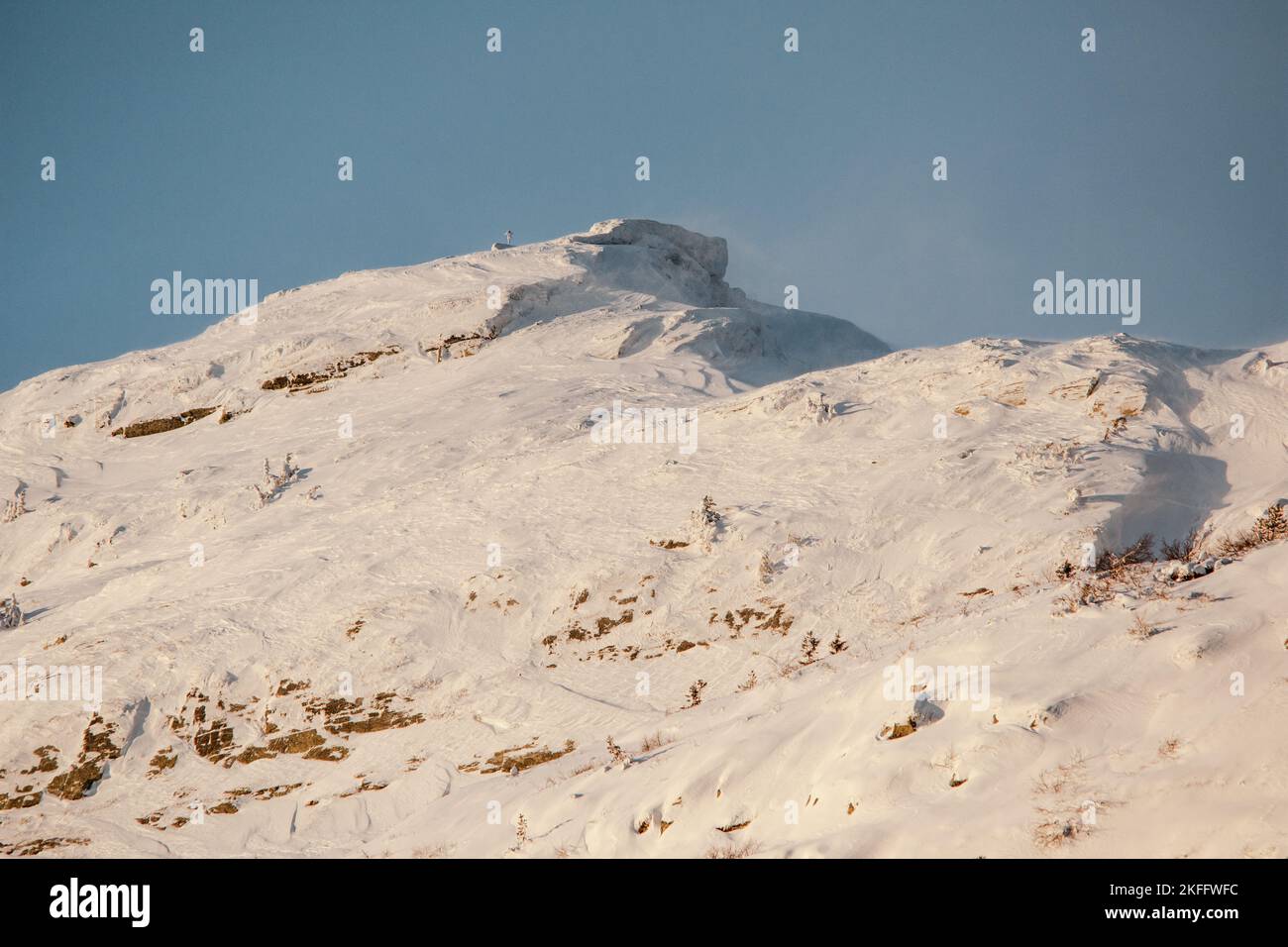 A low-angle of a sunlit snowy mountain against a clear sky background ...