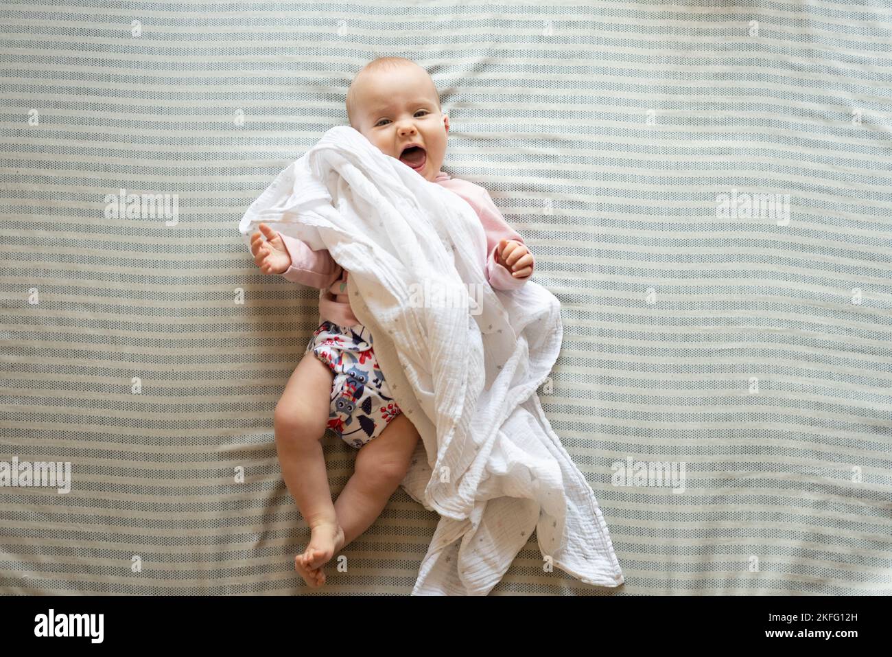 A happy, content baby girl lying on her back. She is wearing a modern ...