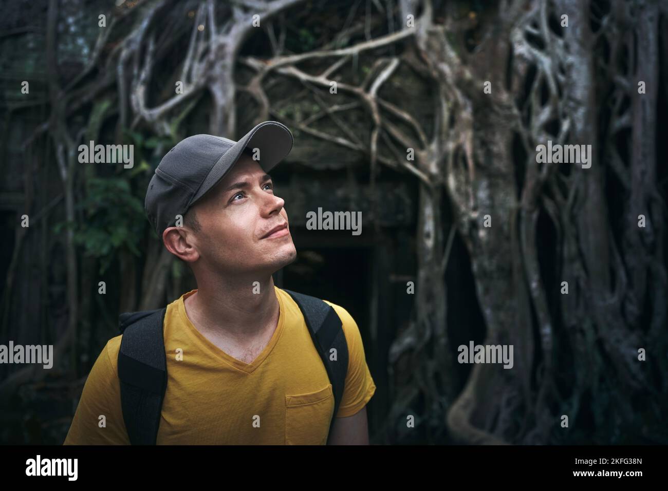 Man admiring overgrown ancient temple under giant roots of tree ...