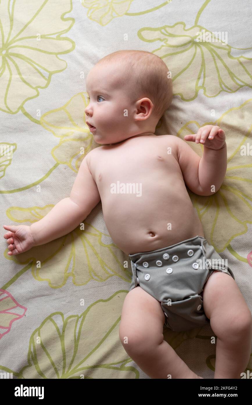 A happy, content baby girl lying on her back. She is wearing a modern ...