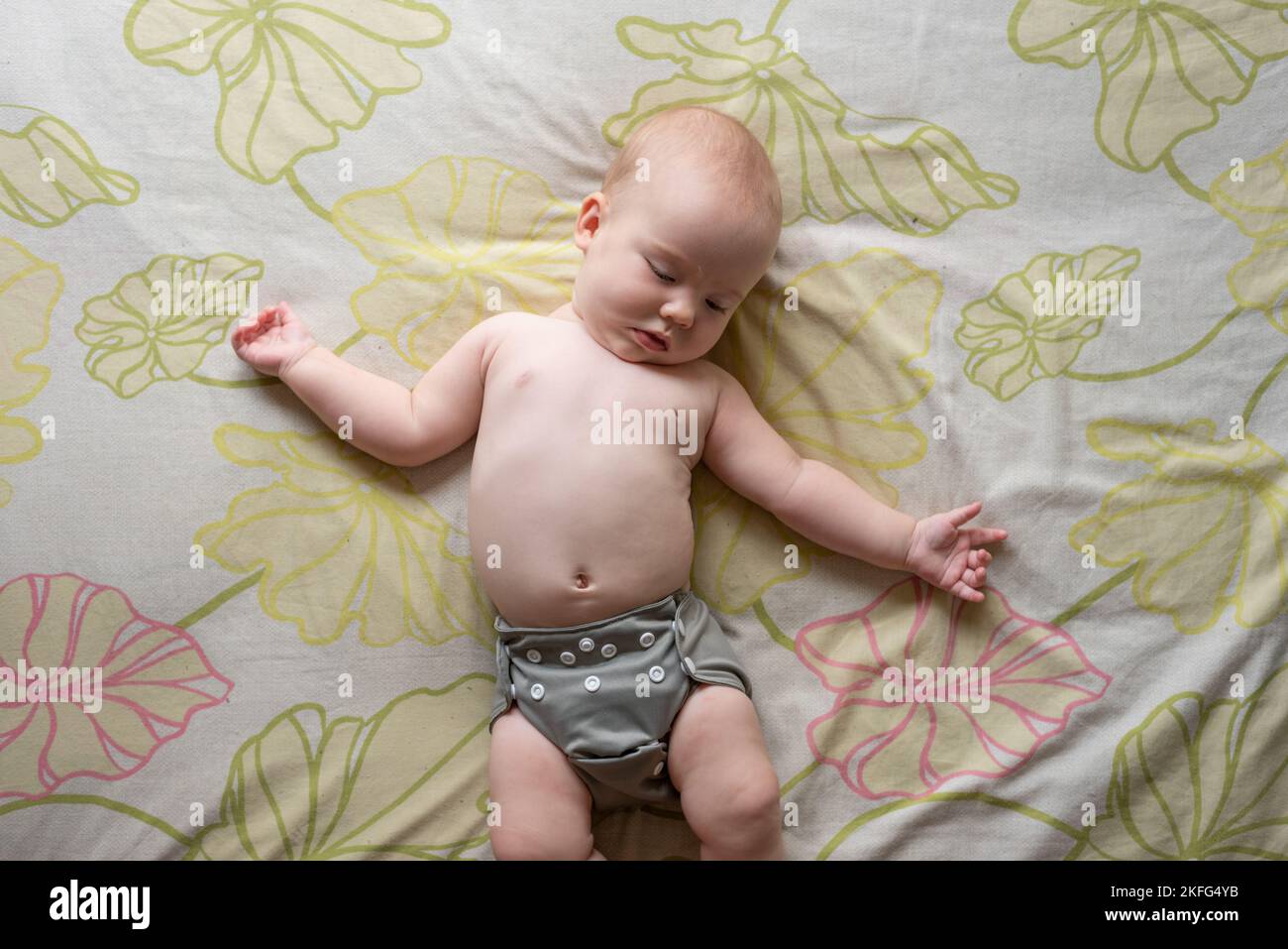 A happy, content baby girl lying on her back. She is wearing a modern ...