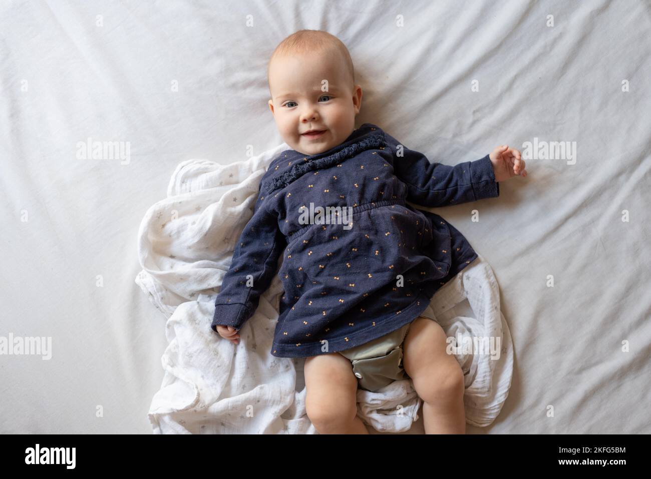 A happy, content baby girl lying on her back. She is wearing a modern ...