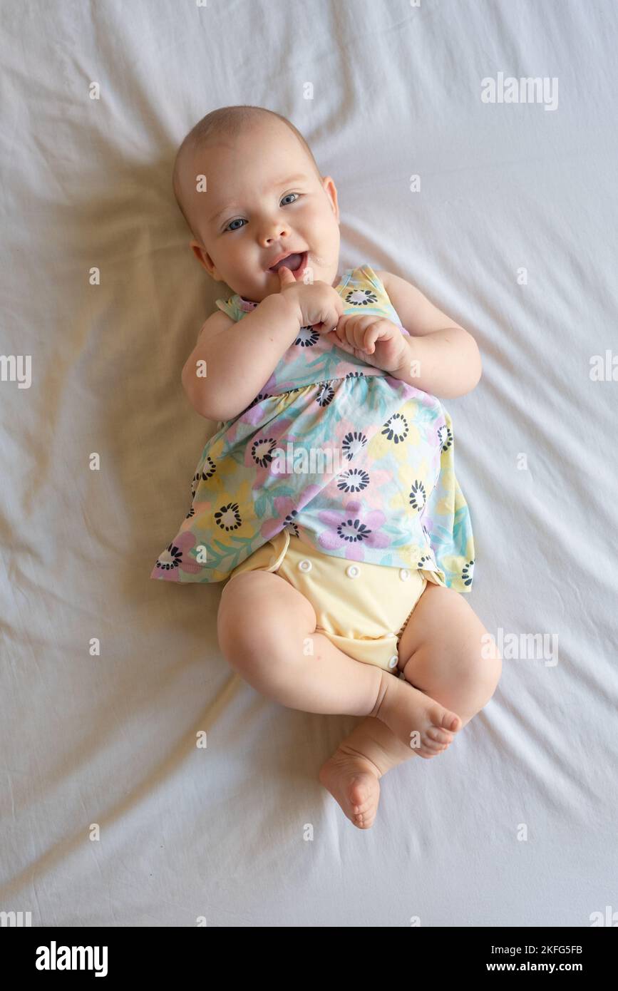 A happy, content baby girl lying on her back. She is wearing a modern ...