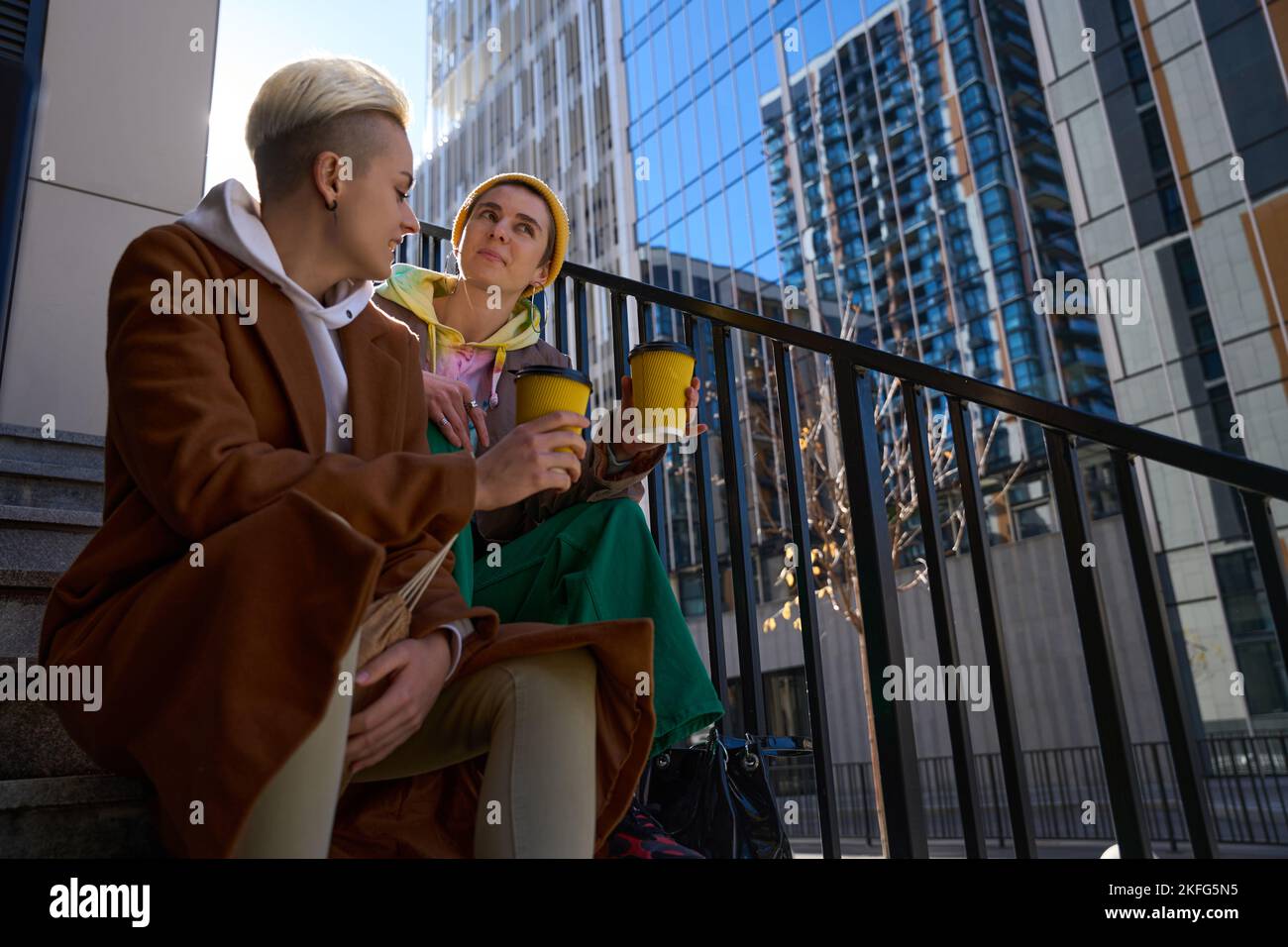 Brunette and blonde sit on steps with yellow cups in hands Stock Photo ...