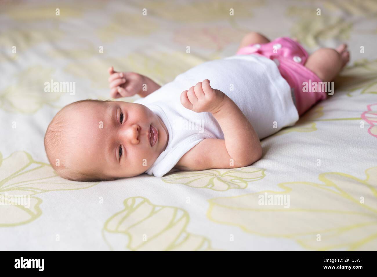 A happy, content baby girl lying on her back. She is wearing a modern ...
