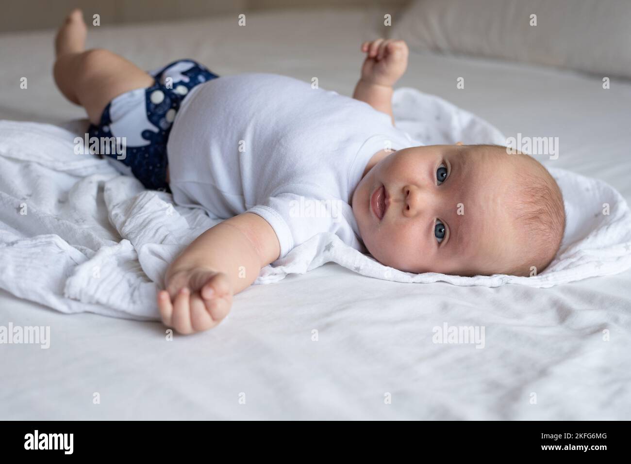 A happy, content baby girl lying on her back. She is wearing a modern ...