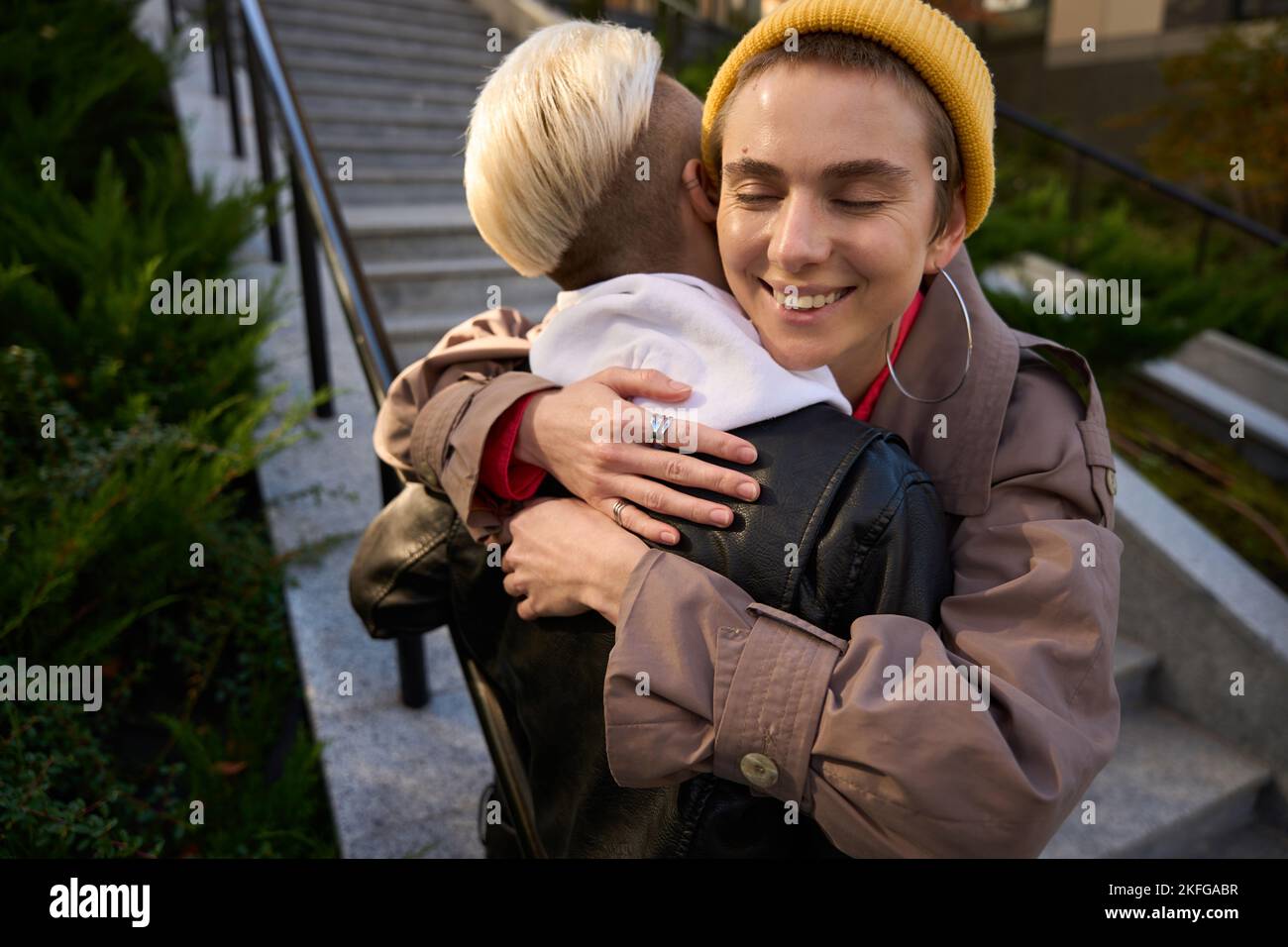 Brunette in a yellow cap warmly hugs her friend Stock Photo - Alamy