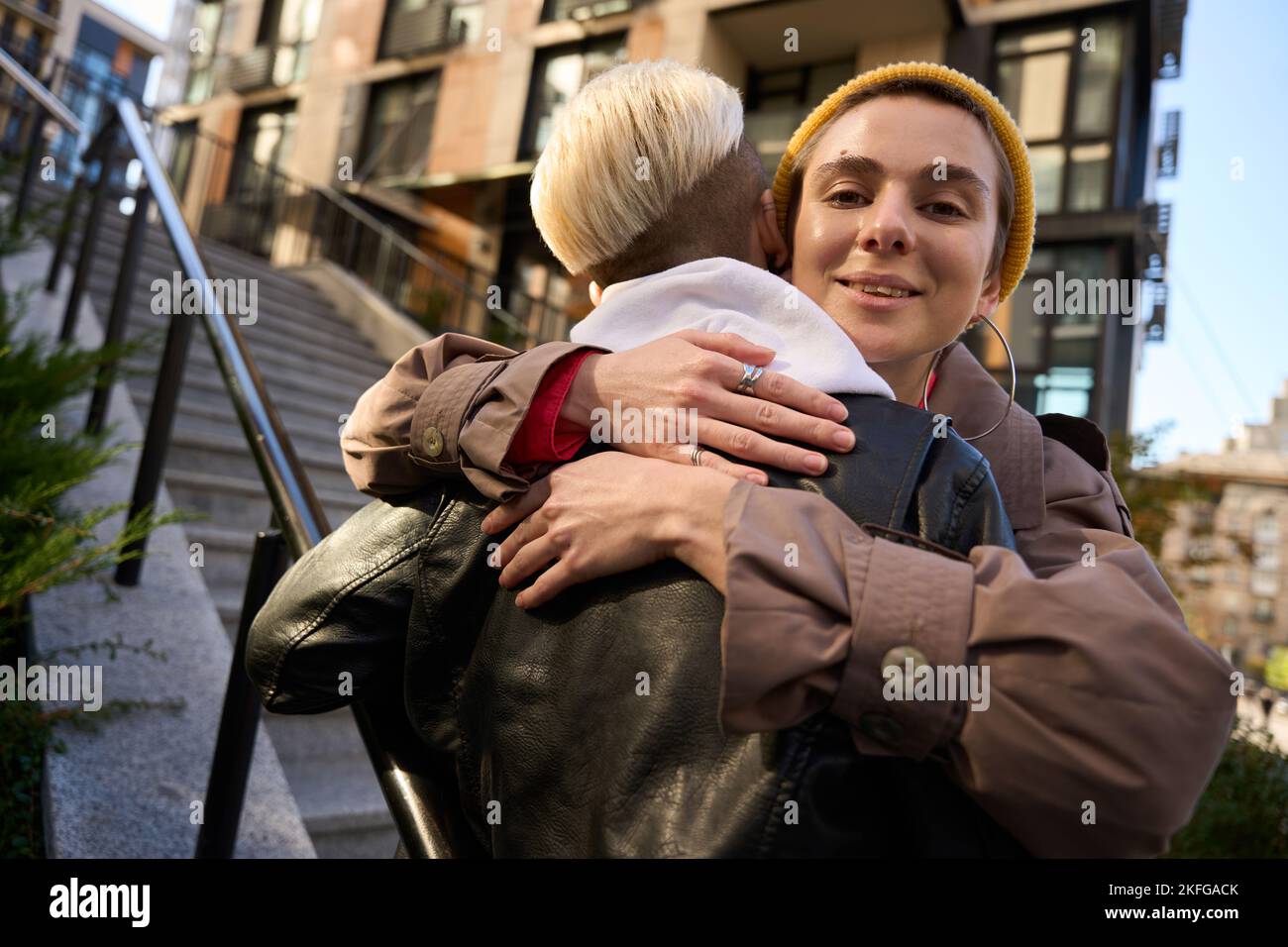Cute brunette in beige trench coat gently hugs her friend Stock Photo ...