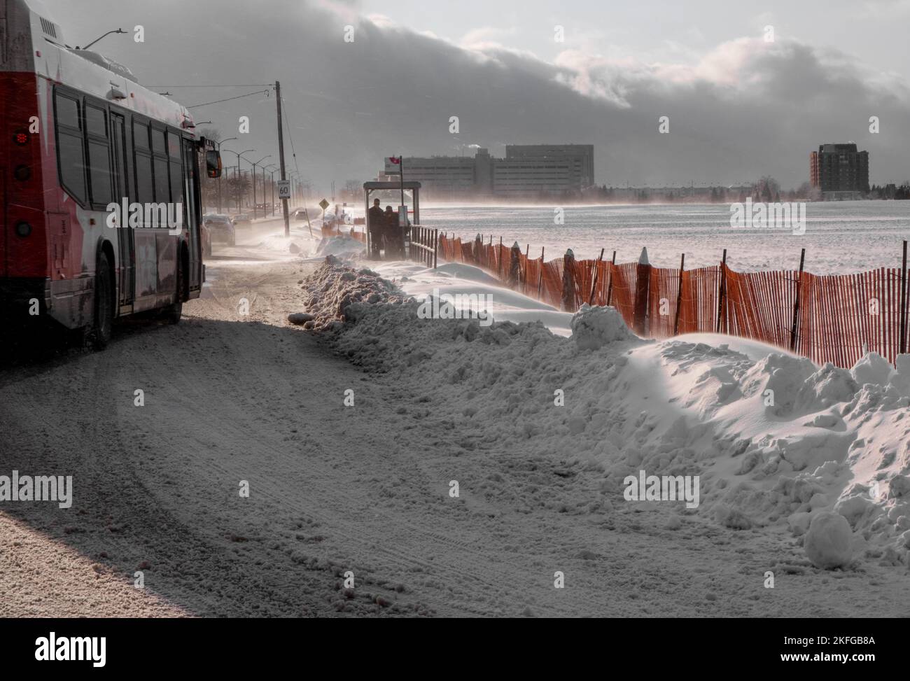 The three people huddle at a bus stop on the edge of a snowy field as a ...