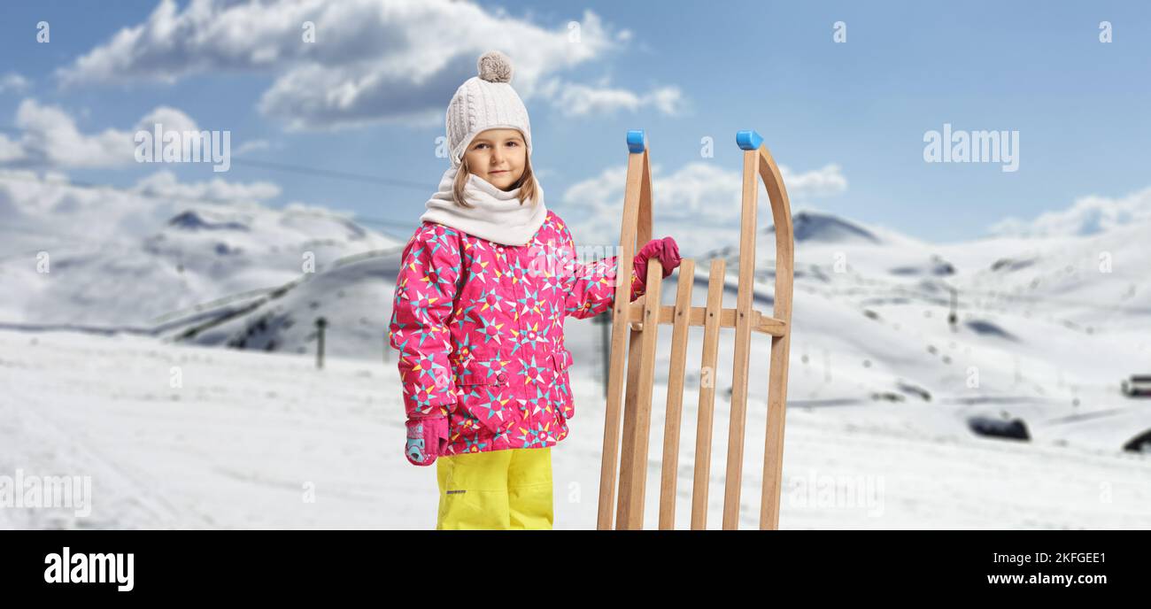 Child in winter clothes standing with a wooden sled on a snowy mountain ...