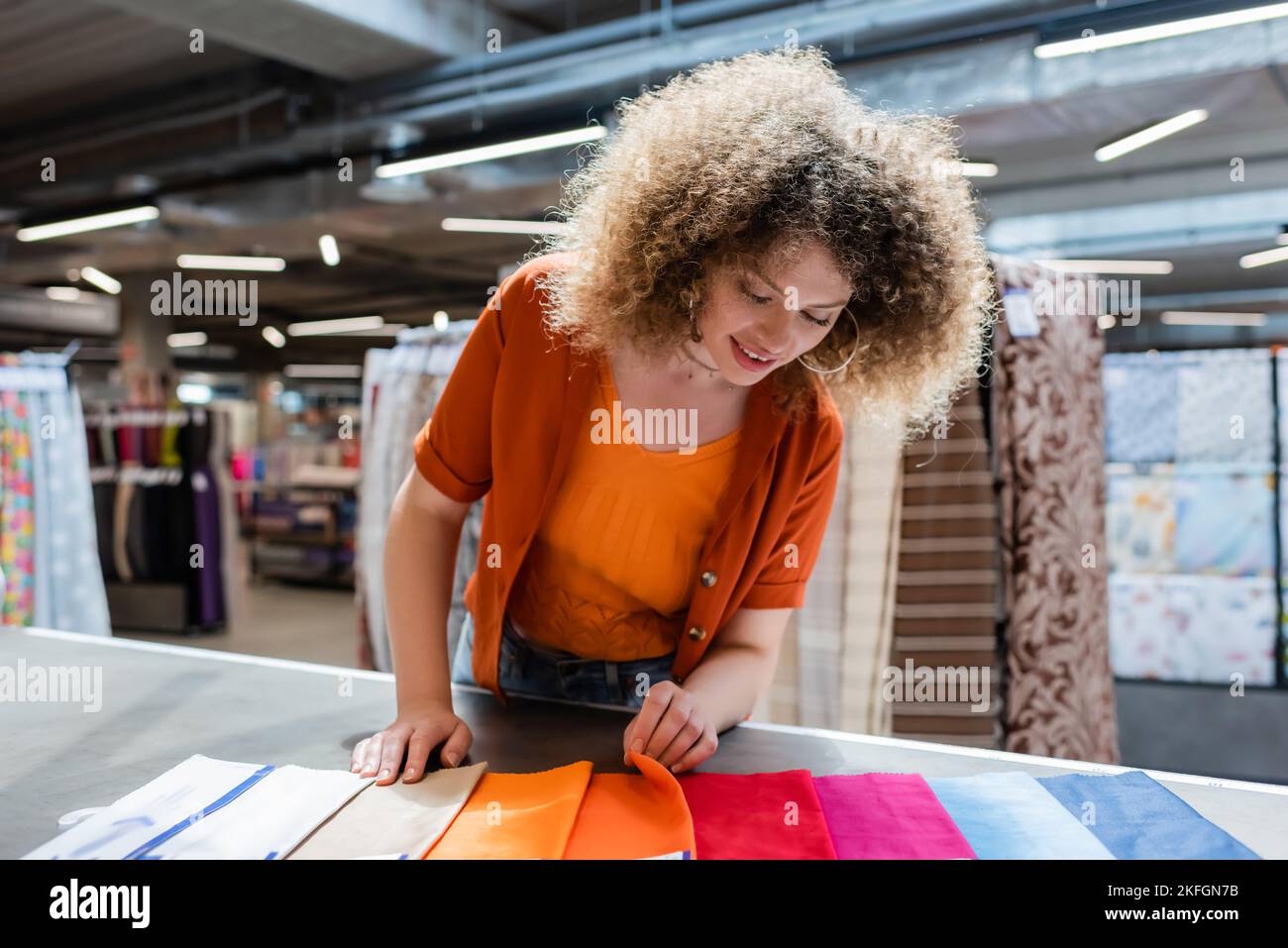 Positive buyer choosing cloth from colorful samples on table in textile ...