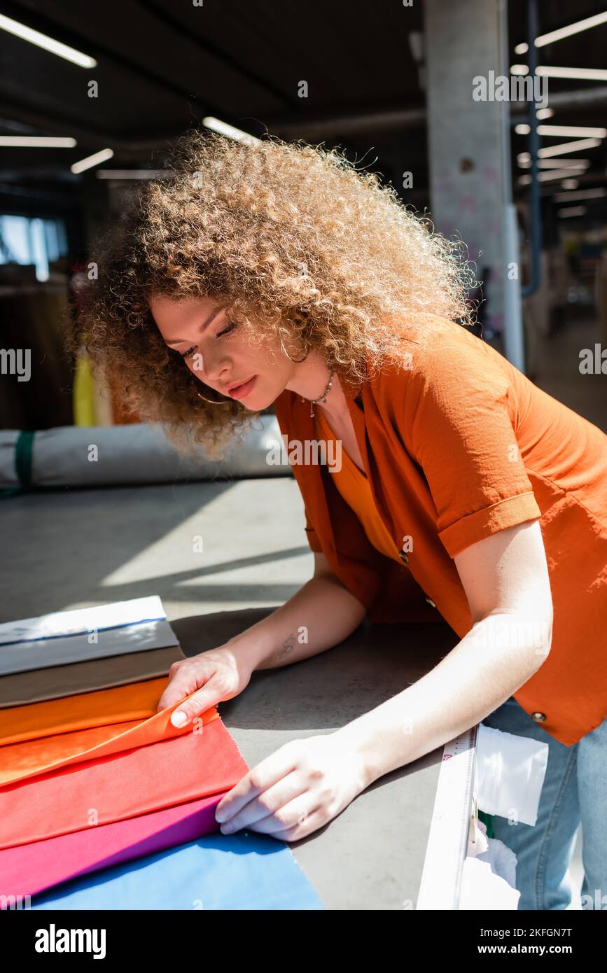 Curly customer holding colorful cloth samples near table in textile ...