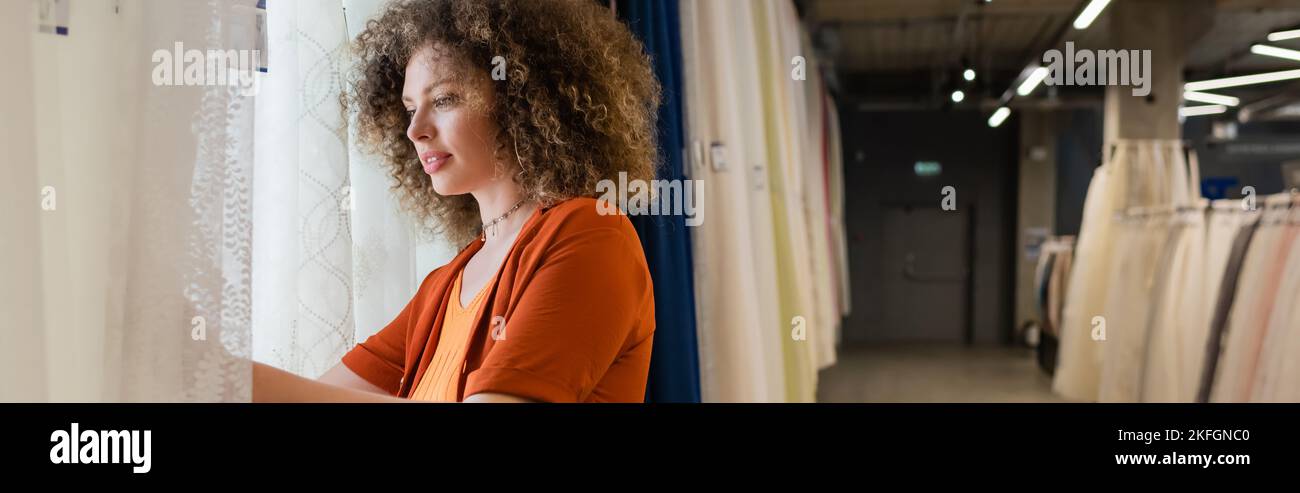 pretty young woman choosing from assortment of curtains in textile shop ...