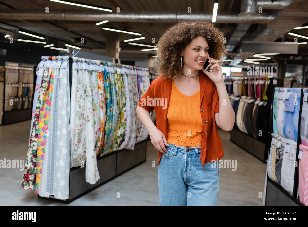 Cheerful customer talking on smartphone in blurred textile shop Stock ...