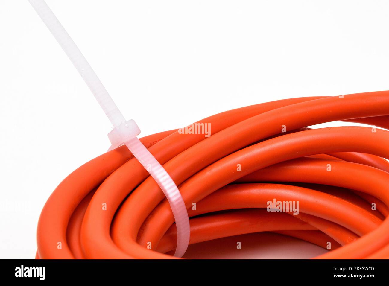 A closeup of a white cable tie tied to a roll of orange cable wire ...