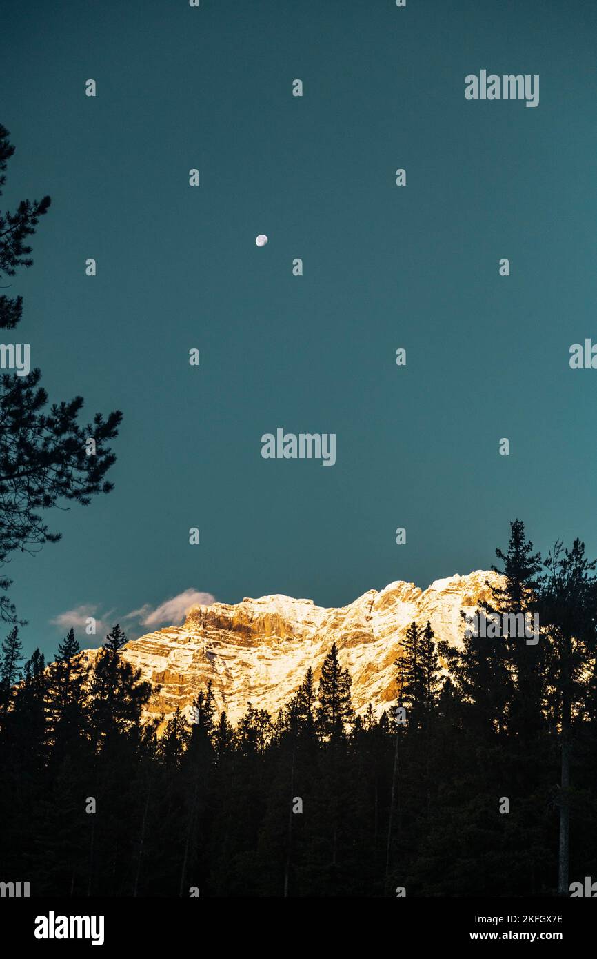 A breathtaking view of a Mount Rundle against a blue sky with a moon ...