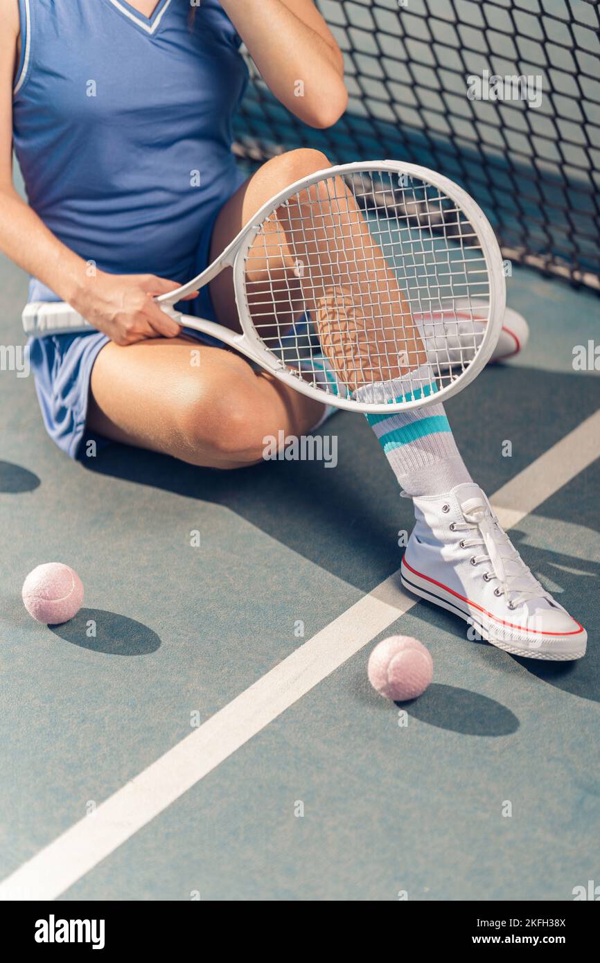 A vertical closeup of a tennis player sitting on the tennis court with ...