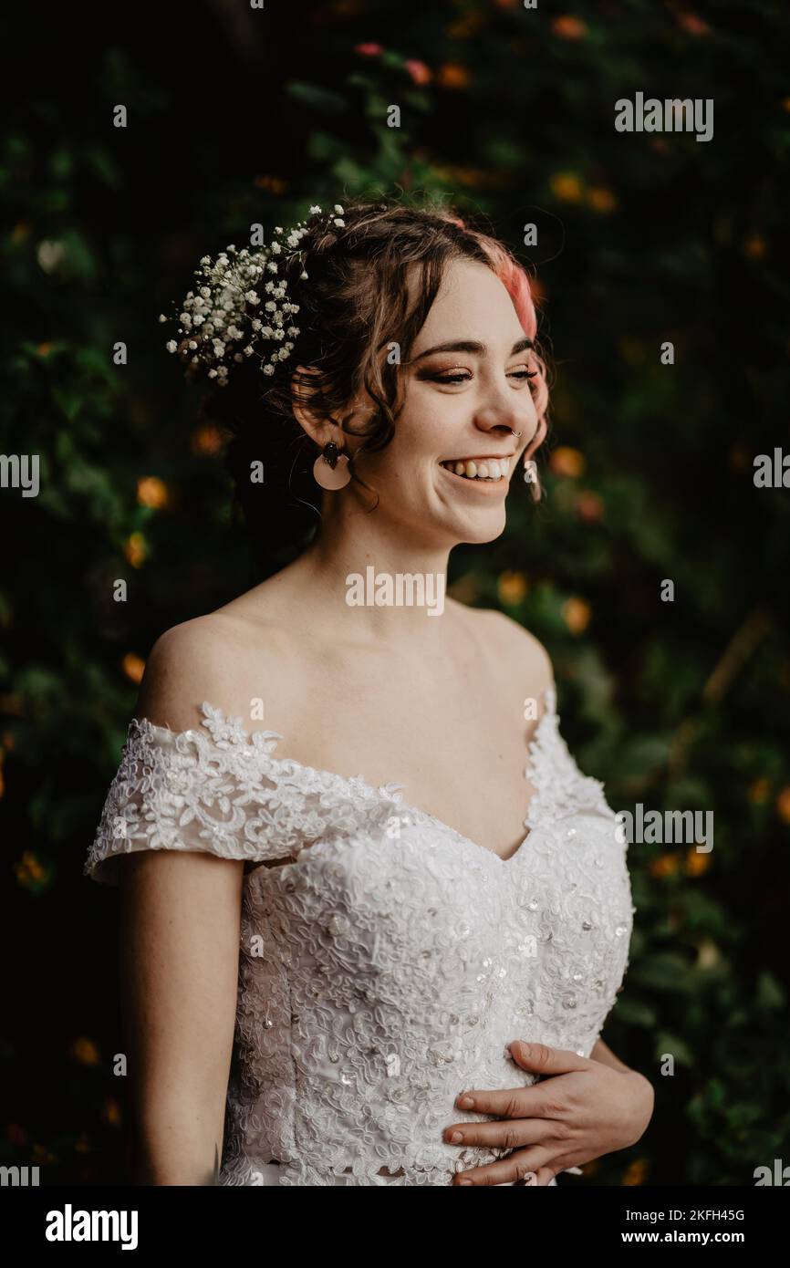A vertical closeup of a happy bride smiling with closed eyes, bushes ...
