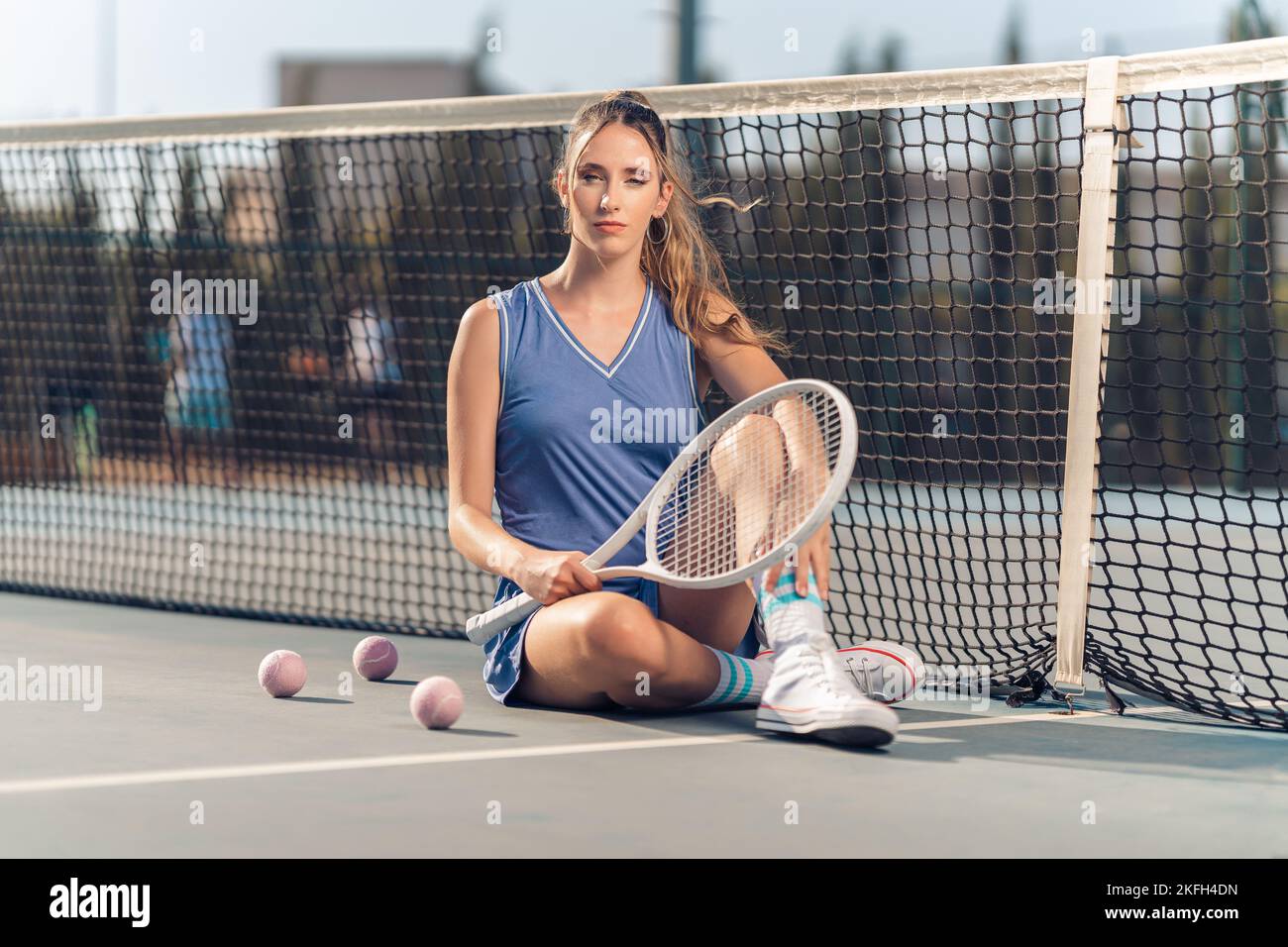 A closeup of a tennis player sitting on the tennis court with balls ...