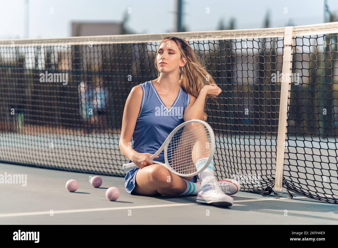 A closeup of a tennis player sitting on the tennis court with balls ...