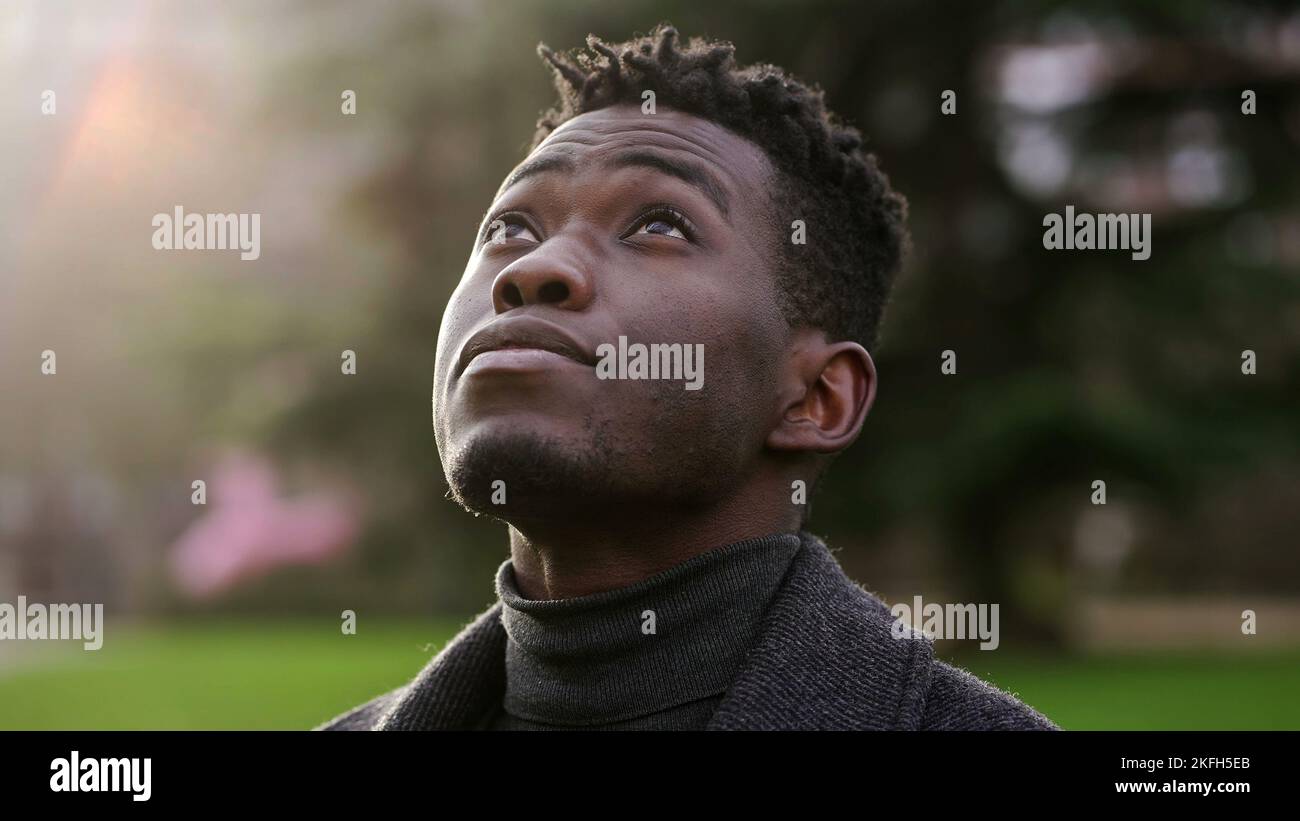 Handsome elegant black African man standing outside at park looking up ...