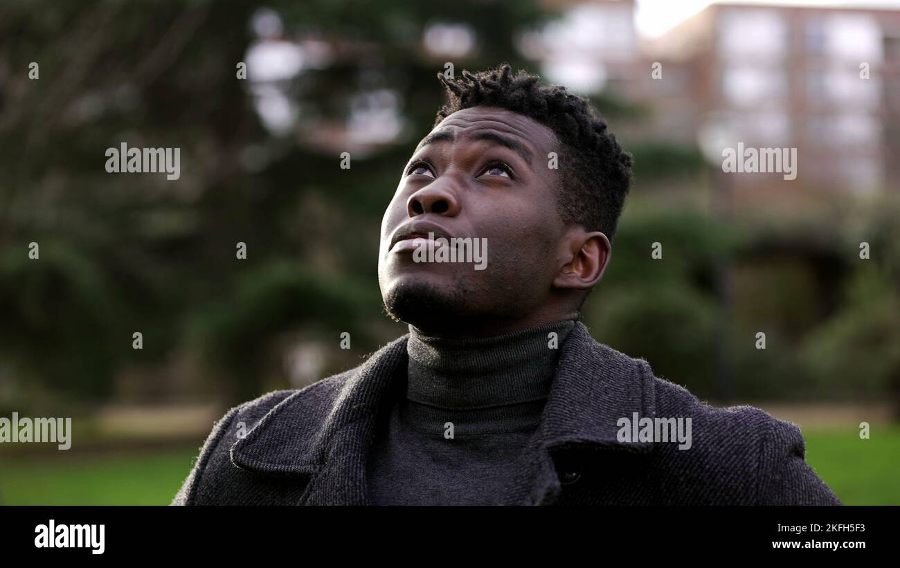 Handsome elegant black African man standing outside at park looking up ...